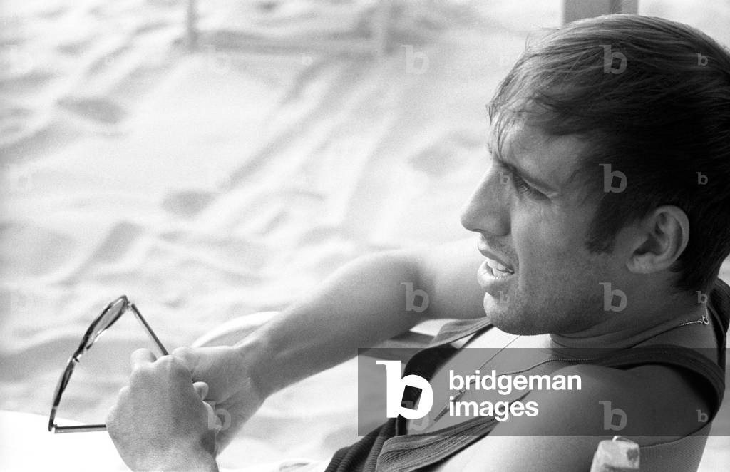 Image of Italian singer and actor Adriano Celentano sitting in a beach