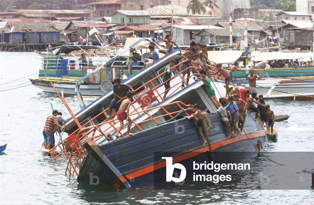 Image of FILIPINO BOYS PLAY AROUND THE HALF SUNK ILL-FATED WOODEN FERRY