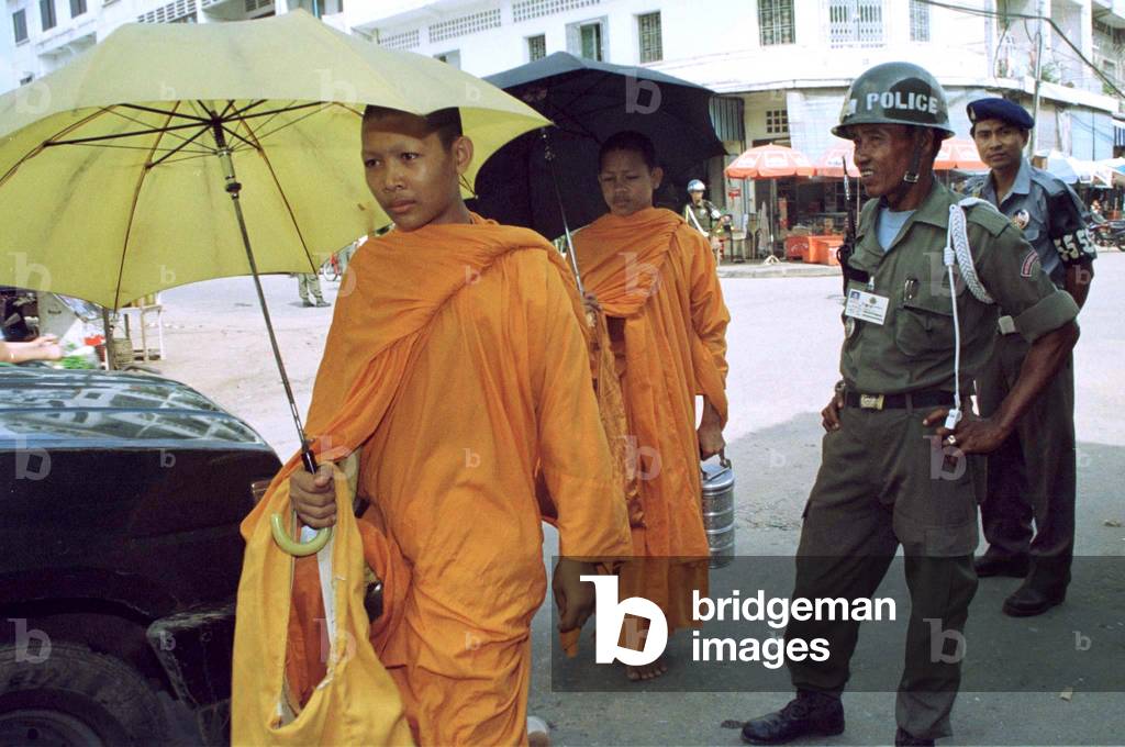 Image of MONKS WALK PAST CAMBODIAN POLICE AT A WEAPONS CHECKPOINT IN