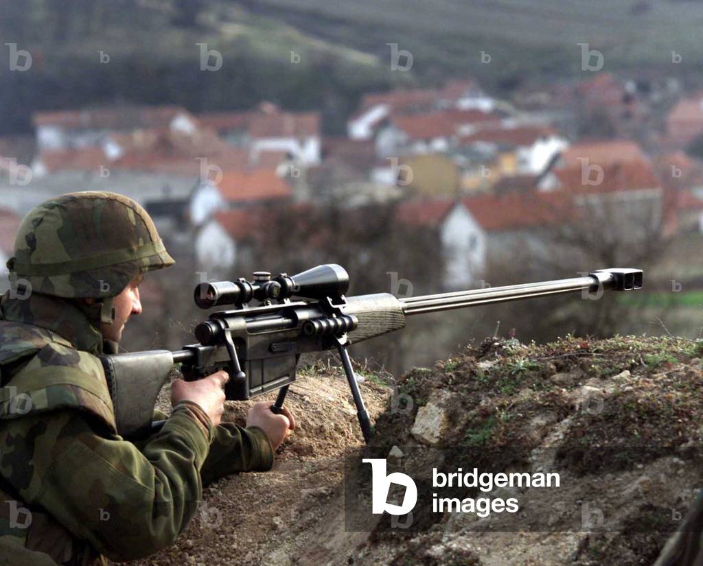 Image of YUGOSLAV ARMY SOLDIER SITS IN A TRENCH WITH A BLACK