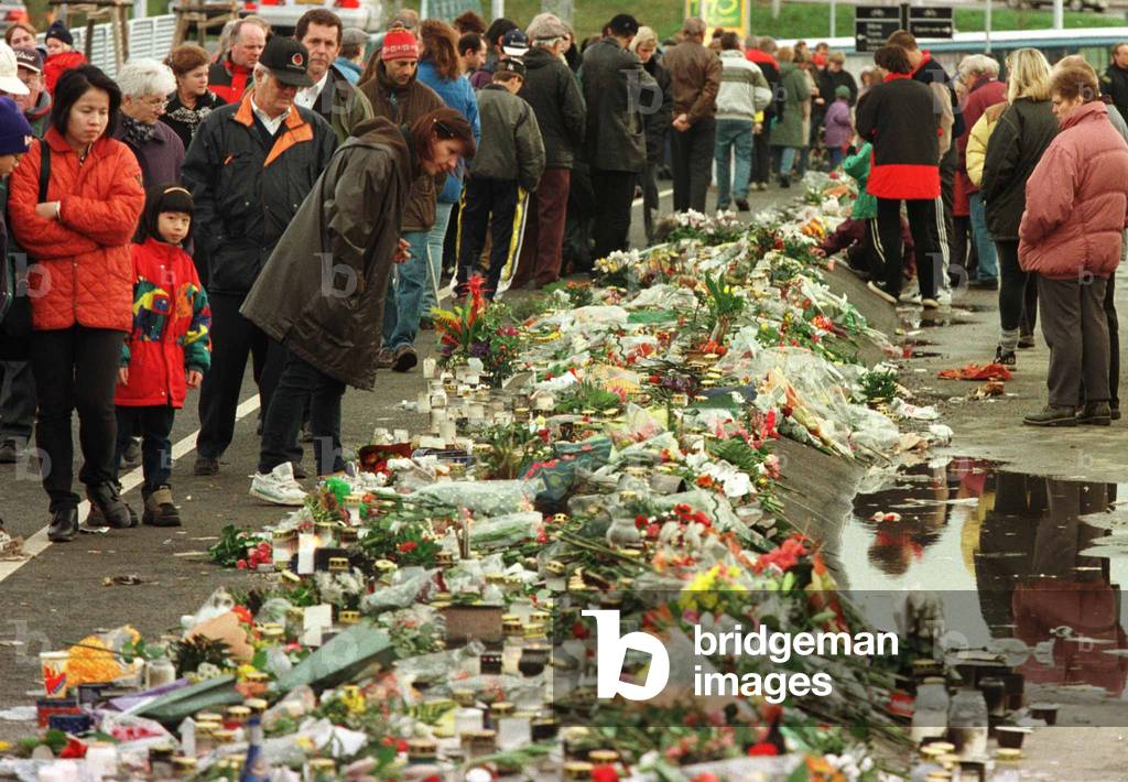 Image of PEOPLE WALK ALONG A LINE OF FLOWERS AND NEAR A