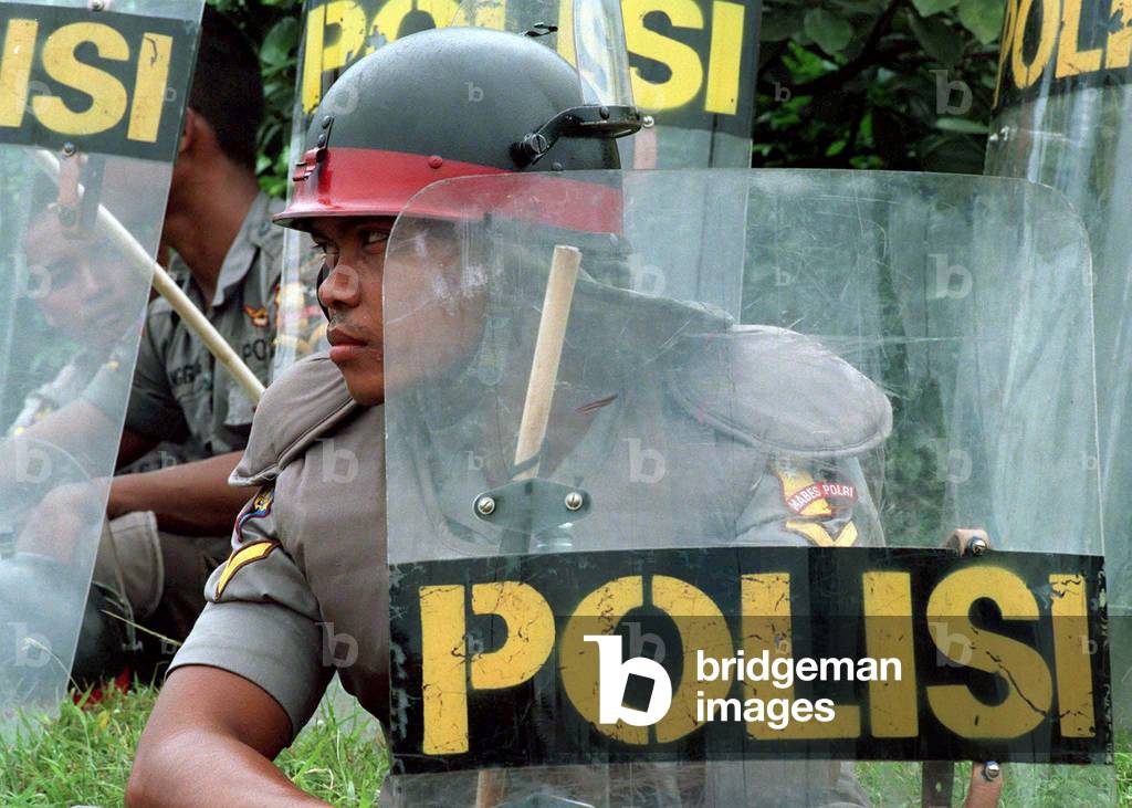 Image of An Indonesian anti-riot policeman sits behind his shield as he