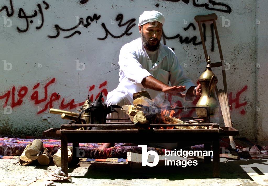 Image of An old Palestinian man makes coffee during the funeral for