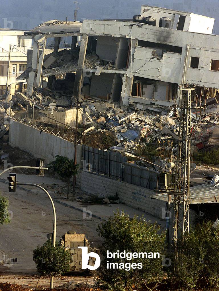 Image of AN ISRAELI APC WAITS OUTSIDE THE DESTROYED COMPOUND OF ...