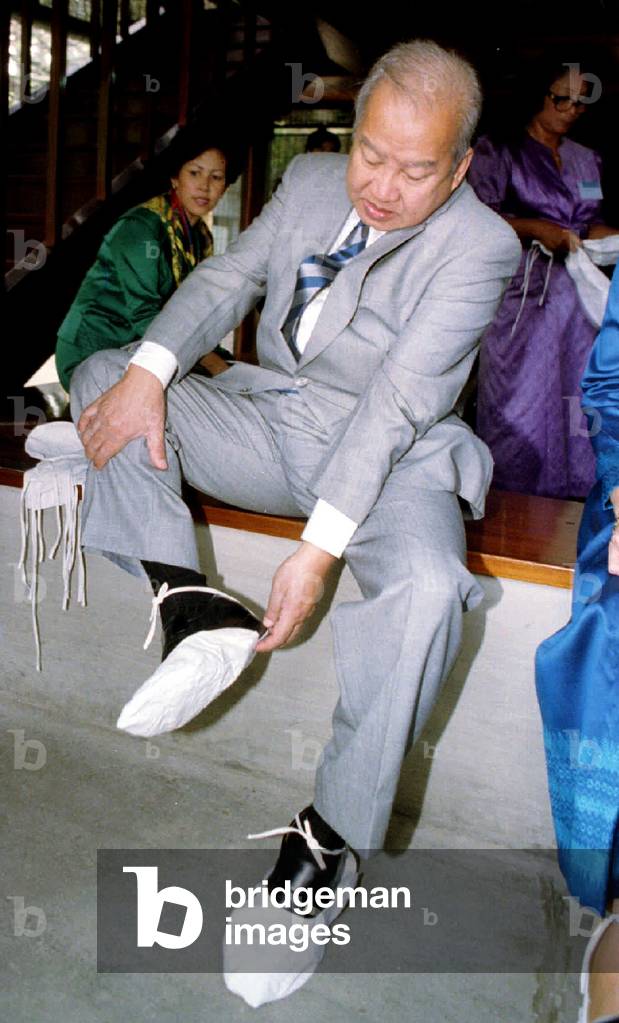 Image of Cambodian King Norodom Sihanouk fixes his shoe cover during a