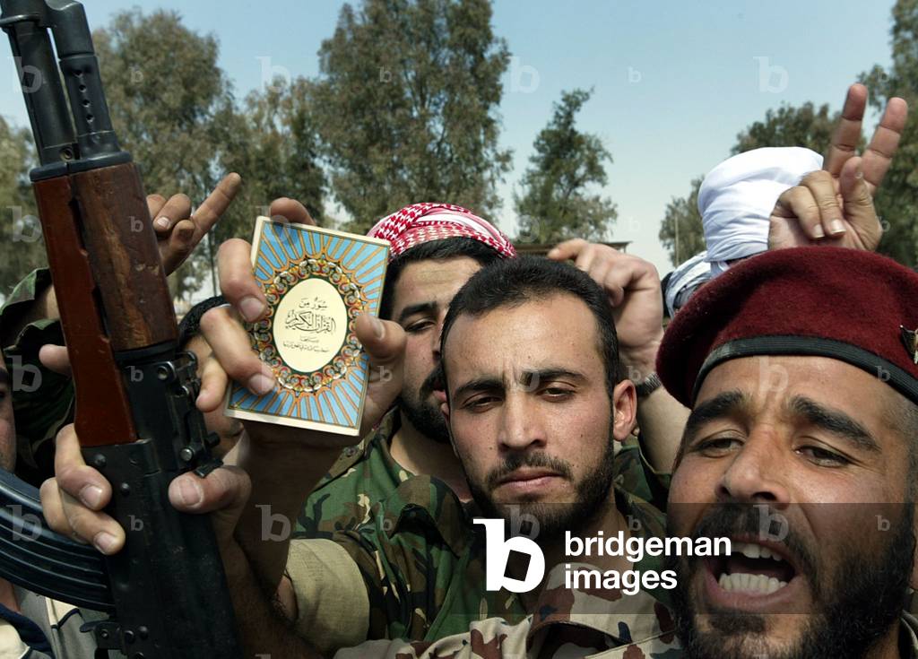 Image of MEMBER OF ARAB VOLUNTEER UNIT HOLDS WEAPON AND KORAN DURING