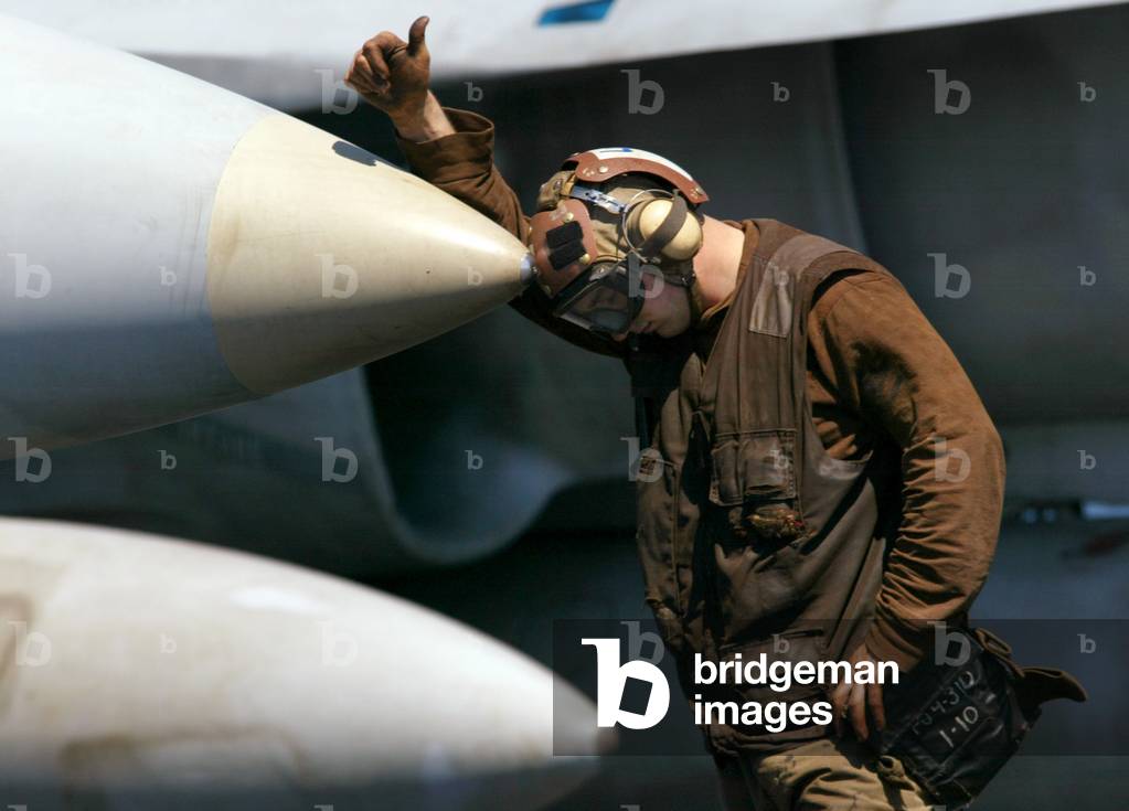 Image of FLIGHT SQUADRON MEMBER LEANS ON NOSE CONE OF F/A-18 HORNET