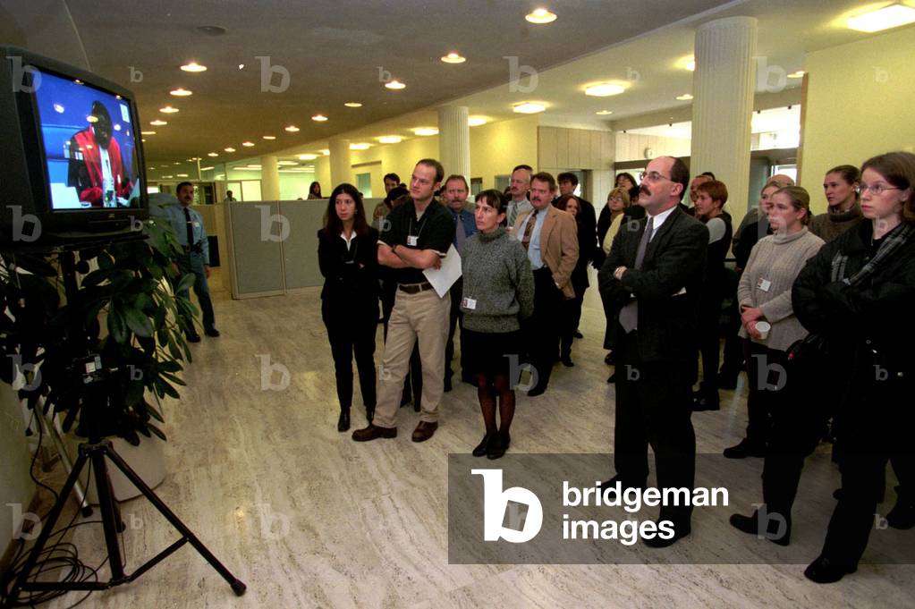 Image of JOURNALISTS AND EMPLOYEES WATCH COURT PROCEEDINGS ON TV SCREEN AT