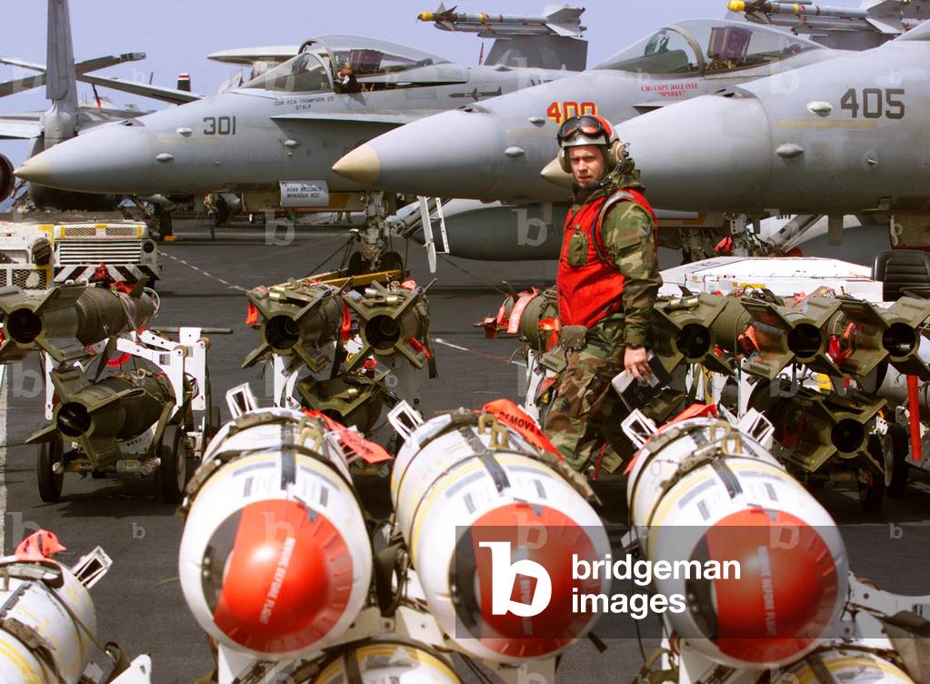 Image of A flight deck crew member walks past bombs and missiles