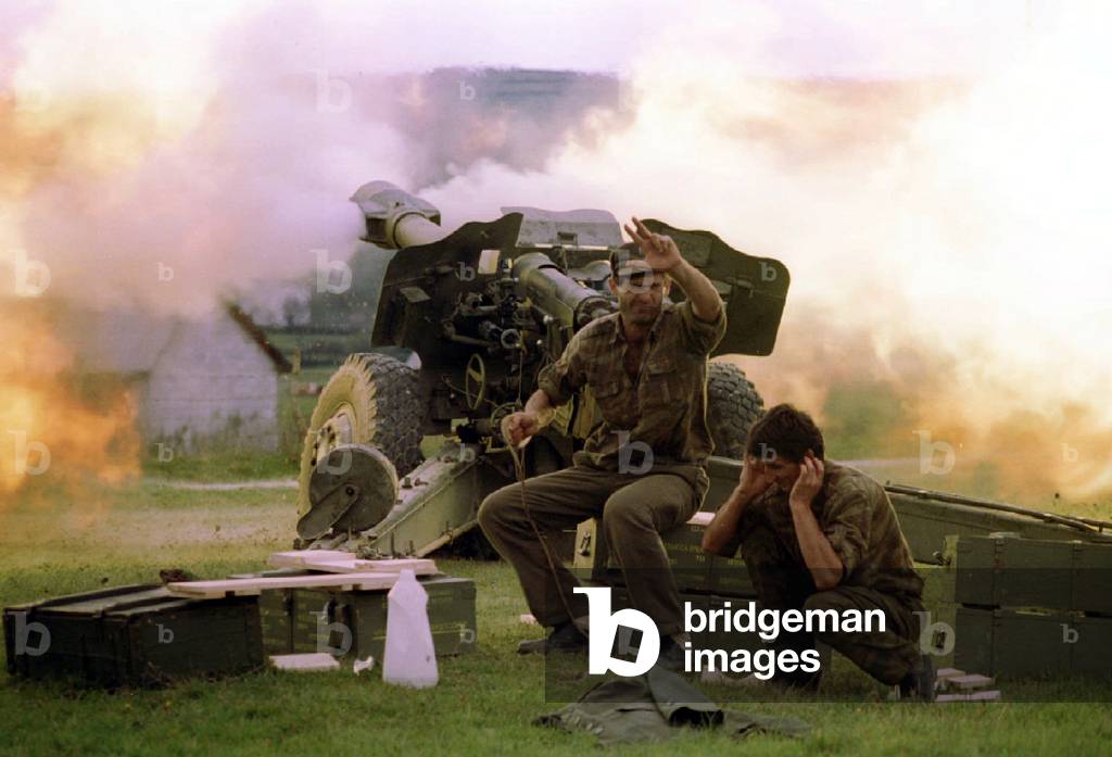 Image of A Bosnian Serb soldier shows three-finger sign while firing a