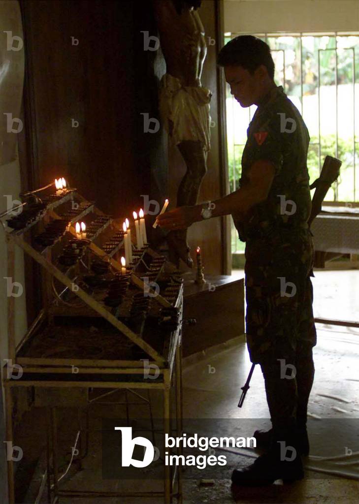 Image of A PHILIPPINE SOLDIER LIGHTS A CANDLE WHILE PRAYING INSIDE THE