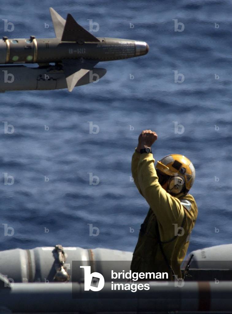 Image of GROUND CREW SIGNALS BELOW A SIDEWINDER MISSILE ON USS ROOSEVELT