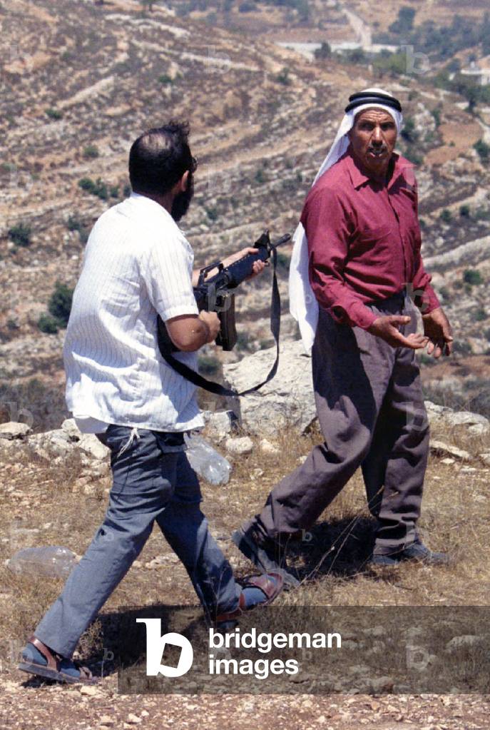 Image of An Israeli settler points his M-16 rifle at a Palestinian