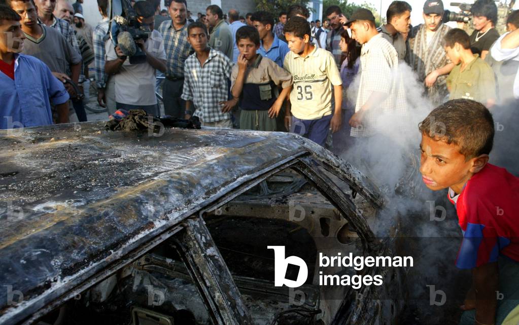 Image of PALESTINIANS CROWD AROUND THE DESTROYED CAR AFTER IT WAS HIT