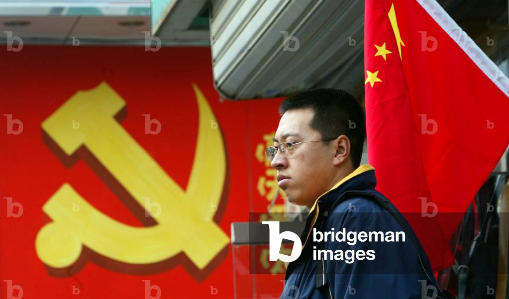 Image of A man stands between a Chinese national flag (R) and
