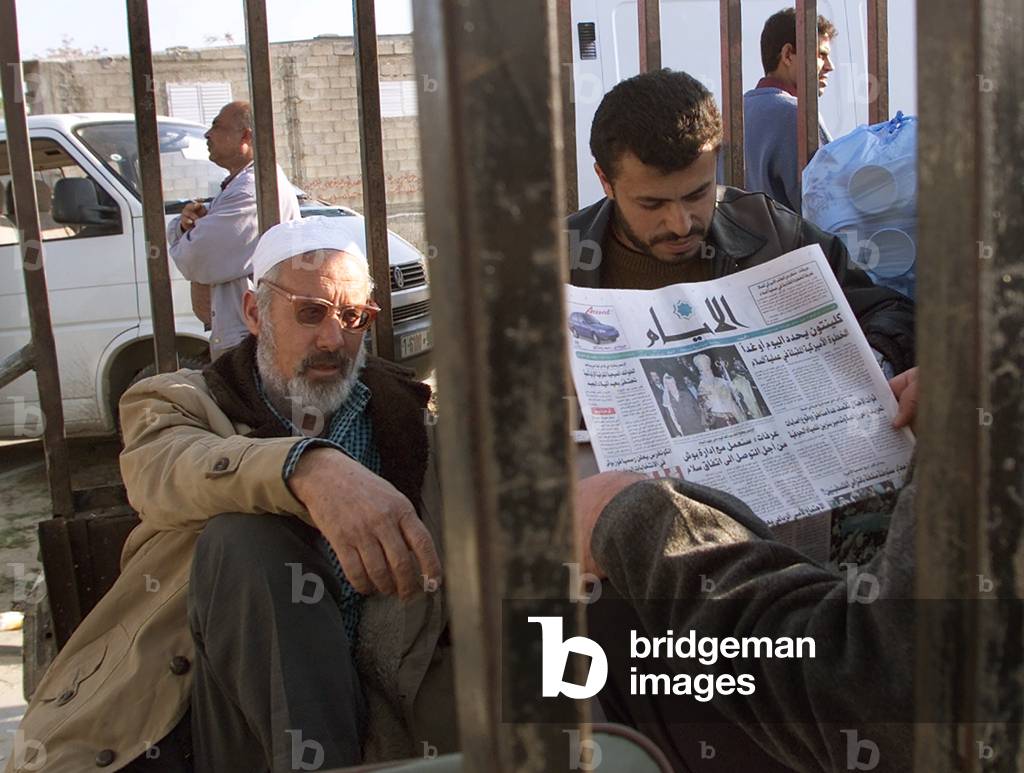 Image of A PALESTINIAN READS NEWSPAPER AS HUNDREDS OF PEOPLE WAIT FOR