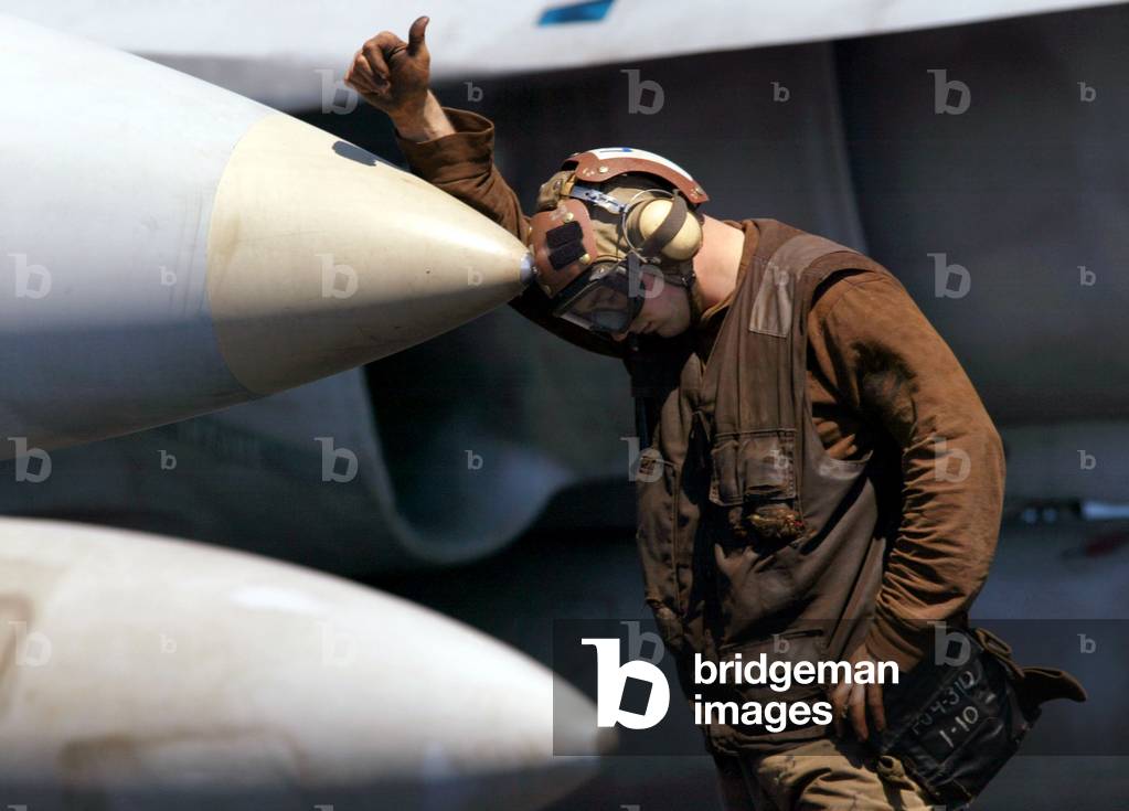 Image of A flight squadron crew member leans on the nose cone