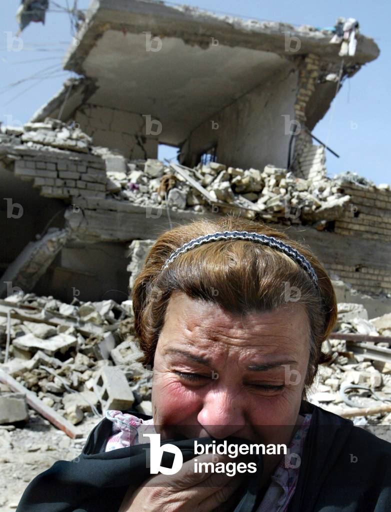 Image of An Iraqi woman sits crying in front of her destroyed