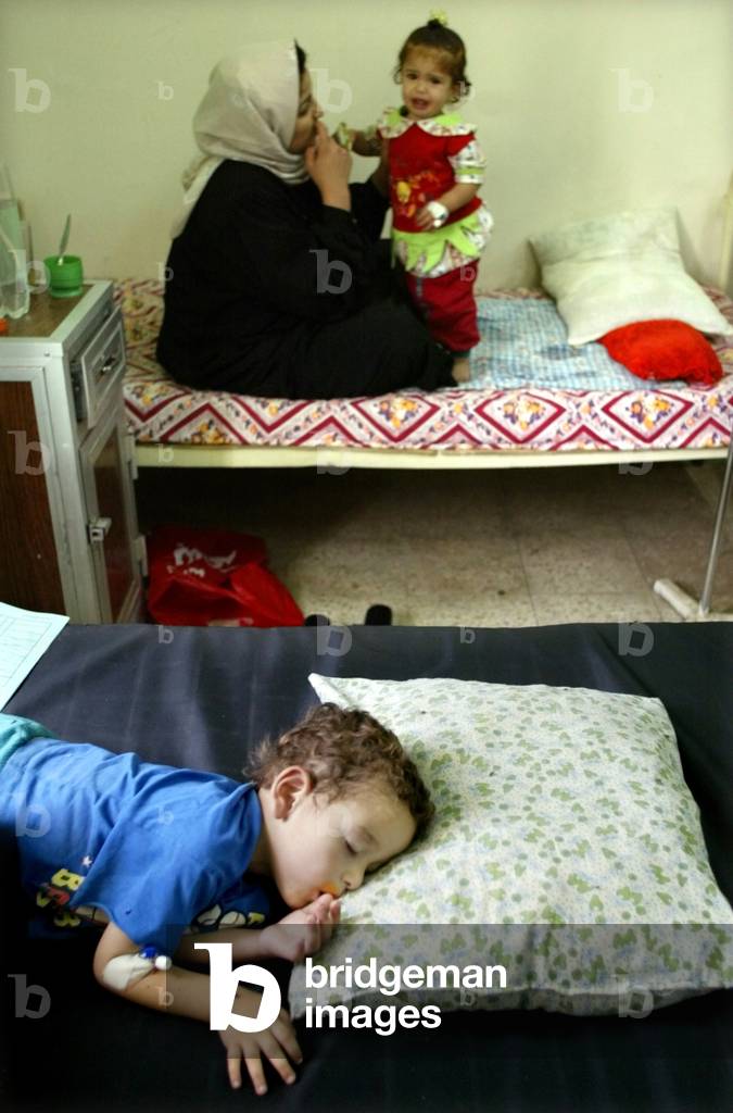 Image of A SICK IRAQI INFANT SLEEPS AS A MOTHER PLAYS WITH