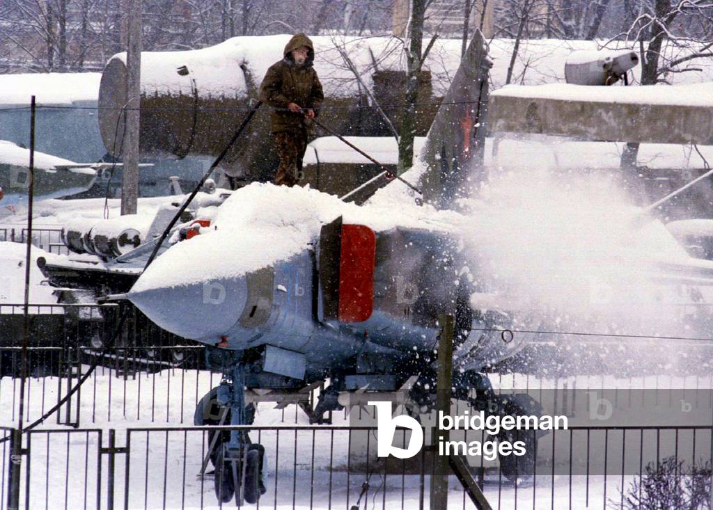 Image of A Russian soldier blows snow from a MIG combat aircraft,