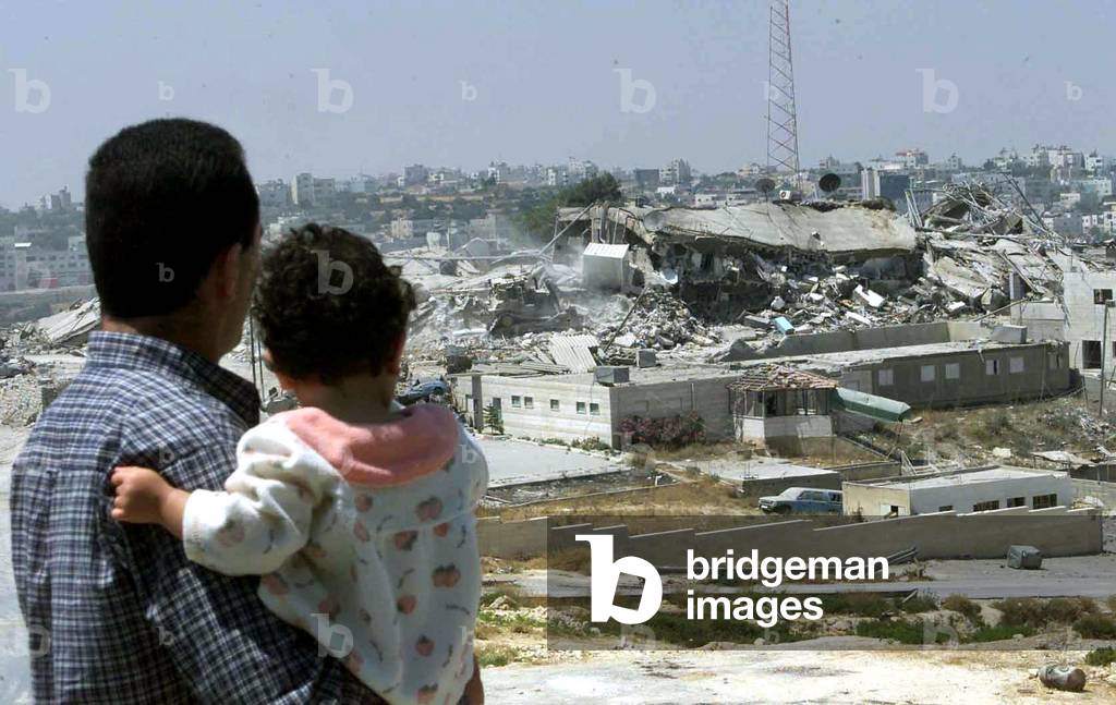 Image of A Palestinian man and child look at the flattened Palestinian