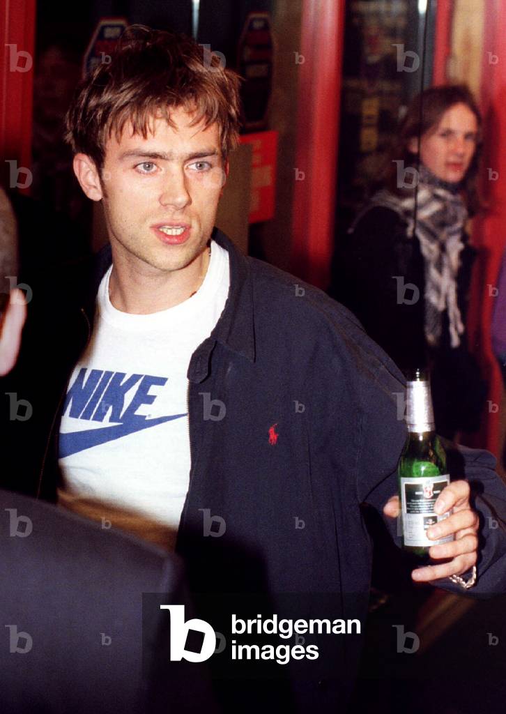 Image of Lead singer of Blur, Damon Alburn carries a bottle of