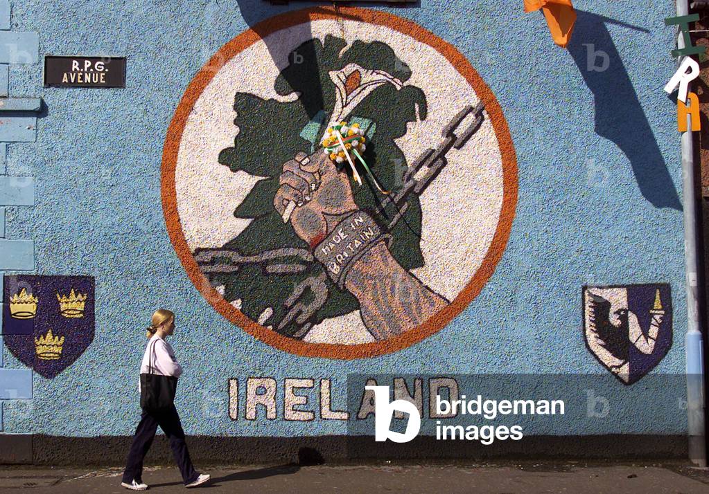 Image of A young girl walks past a Republican mural in a