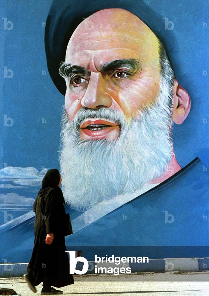 Image of An Iranian woman passes by a billboard featuring the late