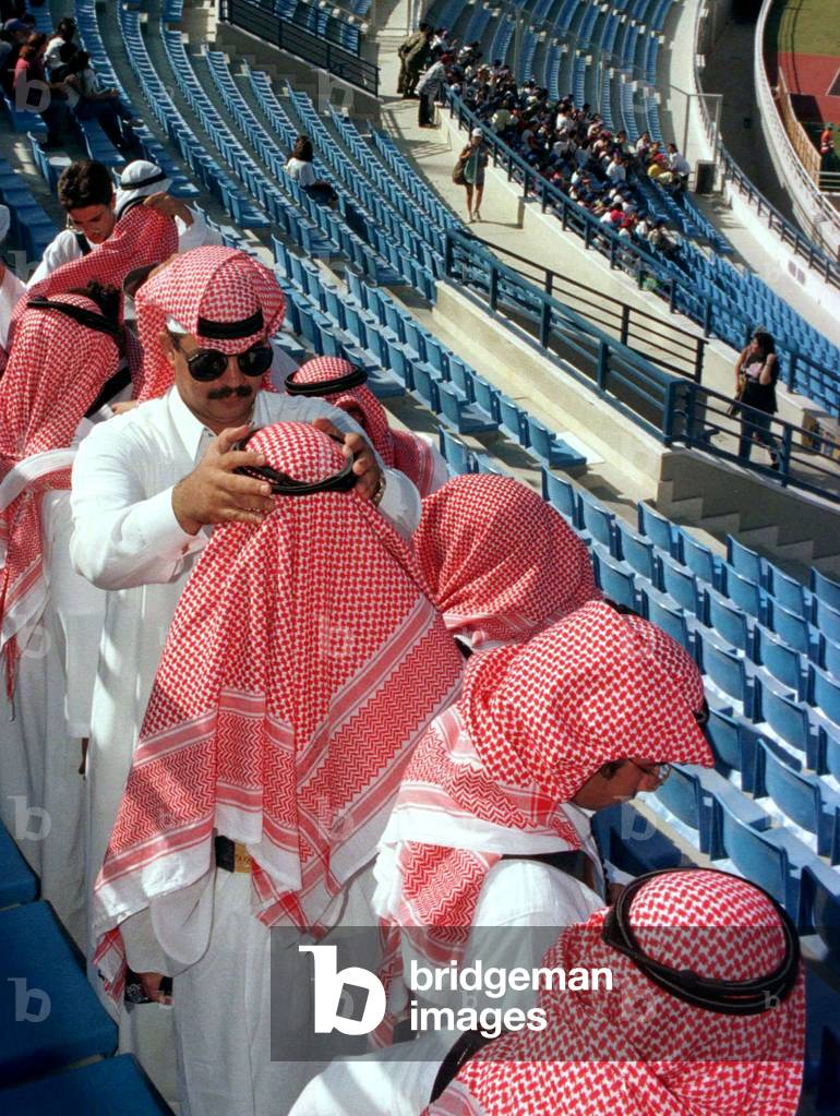 Image of A Saudi athlete dressed in traditional clothes assists ...