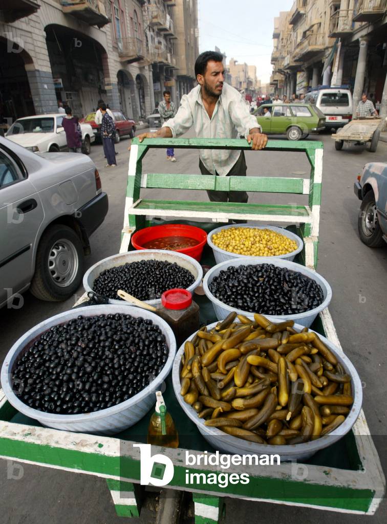 Image of An Iraqi vendor wheels a cart full of olives and