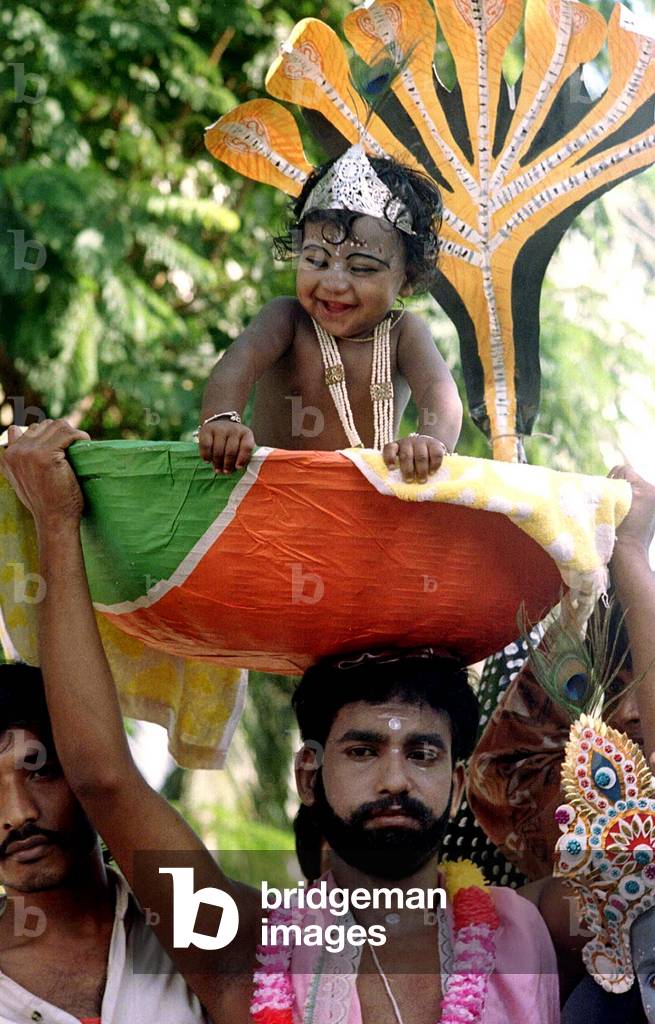 Image of A Hindu devotee carries overhead a small boy dressed like