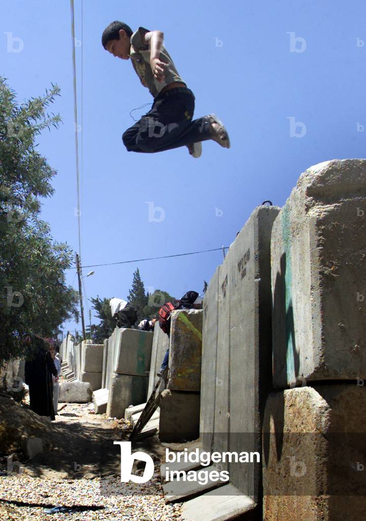 Image of A PALESTINIAN BOY JUMPS OVER A CONCRETE WALL WHICH SEPERATES