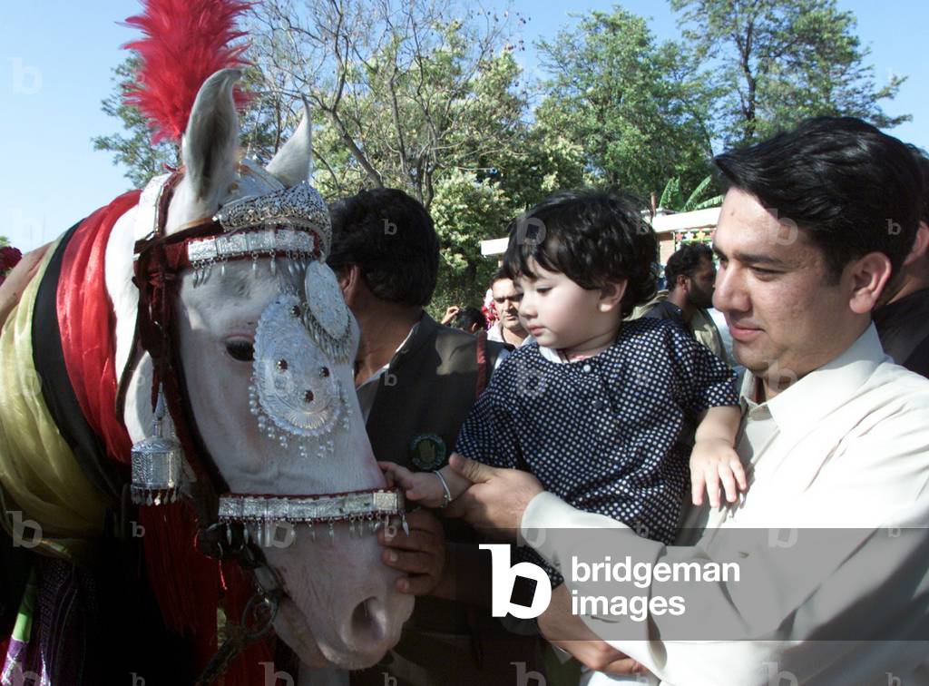 Image of A PAKISTANI SHI'ITE MUSLIM CHILD EMBRACES A SYMBOLIC HORSE DURING