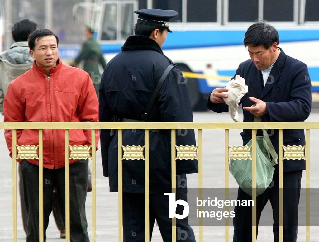 Image of A CHINESE POLICEMAN CHECKS THE CONTENTS OF A MAN'S BAG
