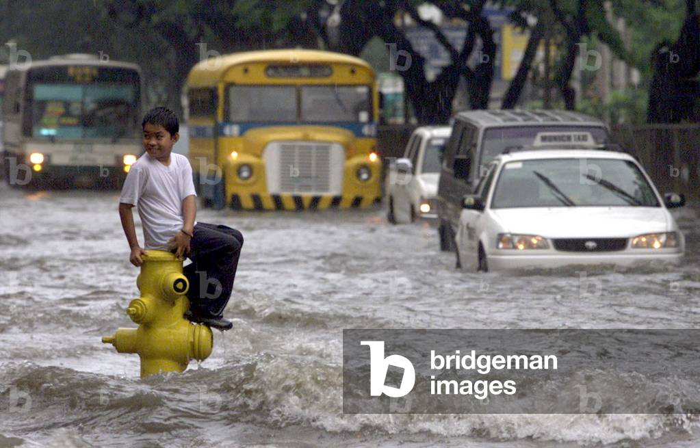 Image of EIN PHILIPPINISCHER JUNGE SITZT AUF EINEM HYDRANTEN, WÄHREND ...