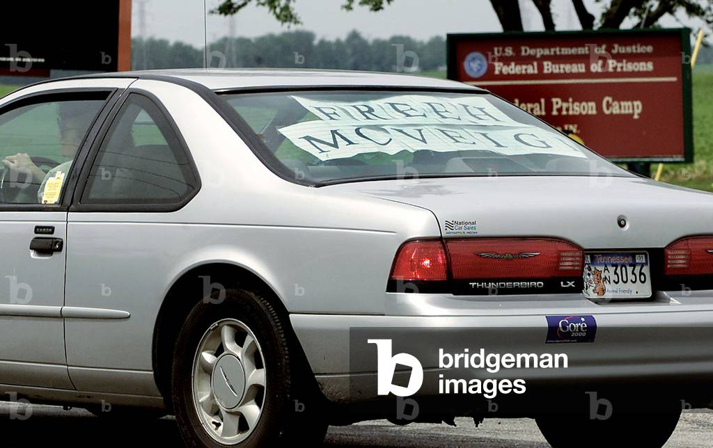 Image of A CAR WITH SIGN IN BACK WINDOW DRIVES PAST PRISON
