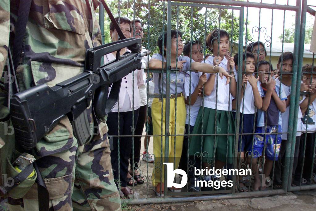 Image of Filipino school children peer through the steel gate of the