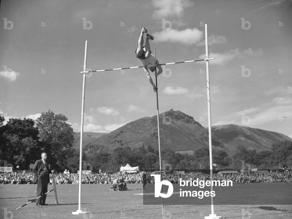 Image of Pole vaulter vaulting over bar with judge watching closely ...