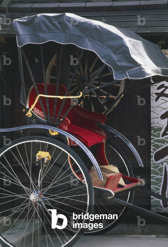 Image of Two-wheeled rickshaw with black canopy, handles resting on ...