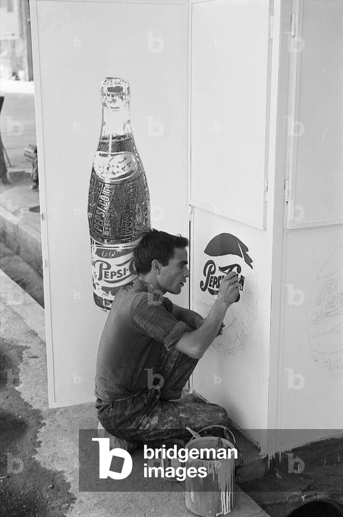 Image of A man painting the Pepsi-Cola logo, Iran, 1964 (b/w photo)