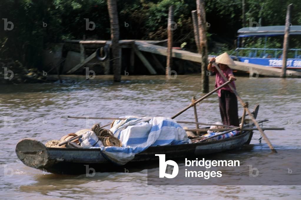 Image of Vietnam, Mekong Delta, woman rowing sampan boat on river with