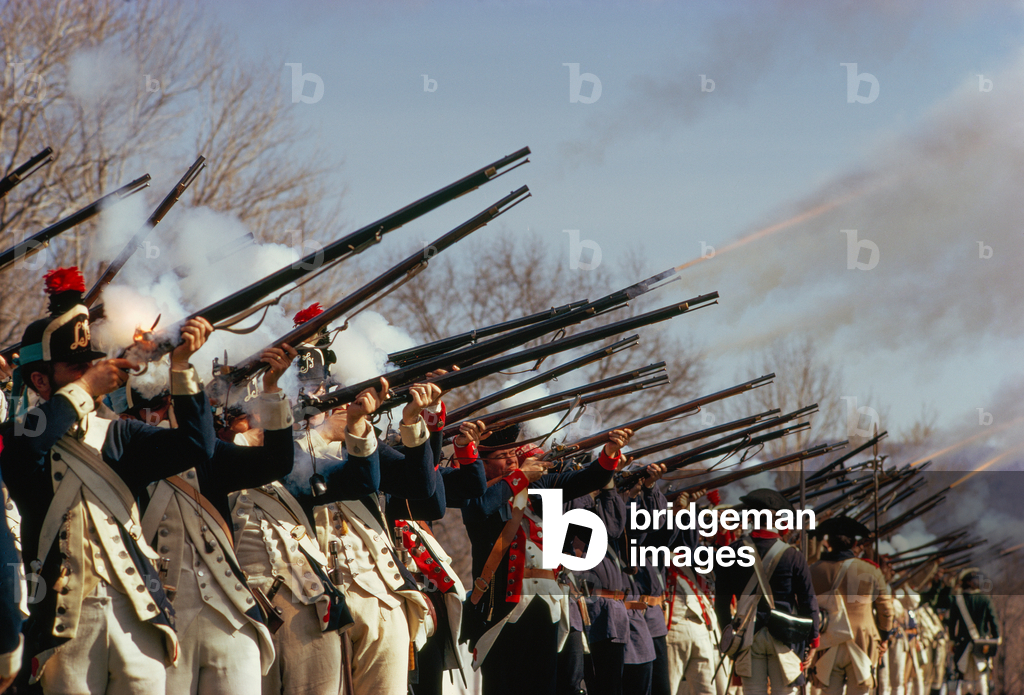 Image of A formation of soldiers fire their muskets during a reenacted ...