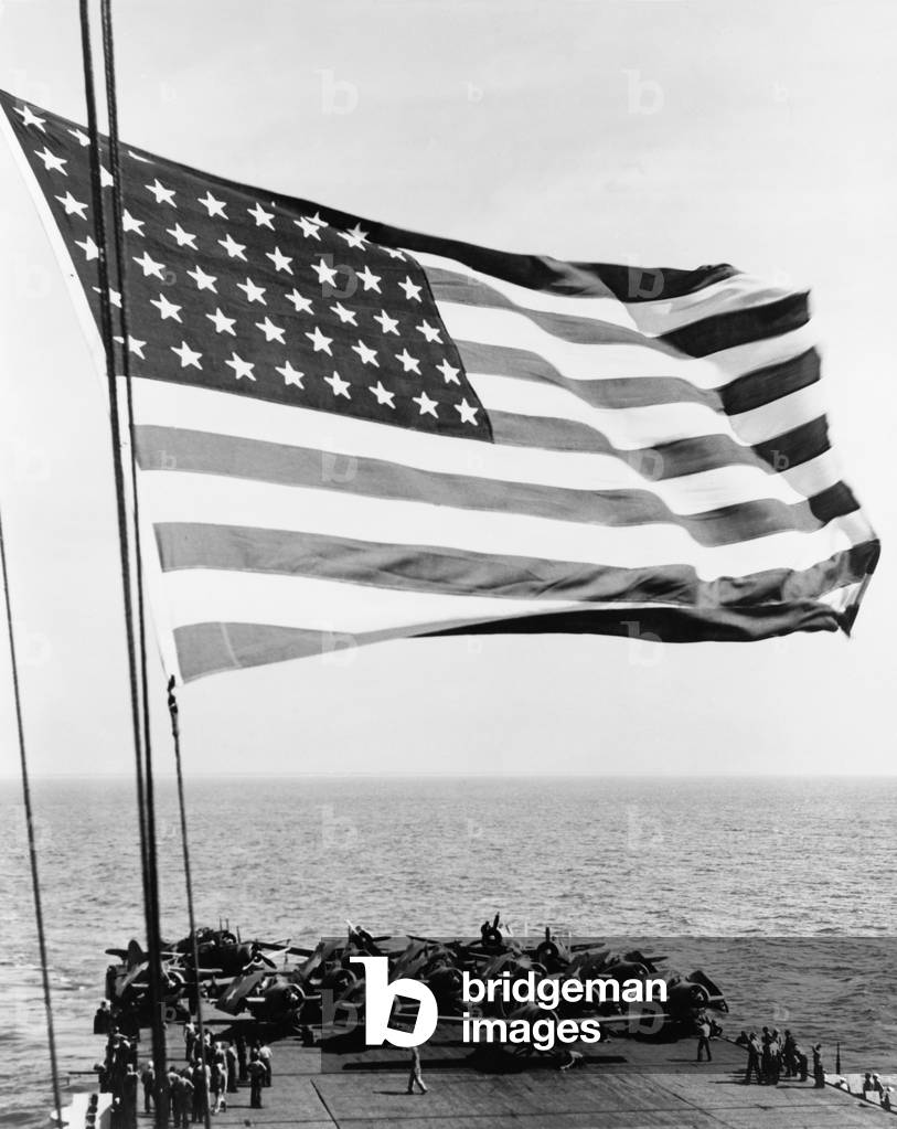 Image of U.S. flag waving in foreground over flight deck of an