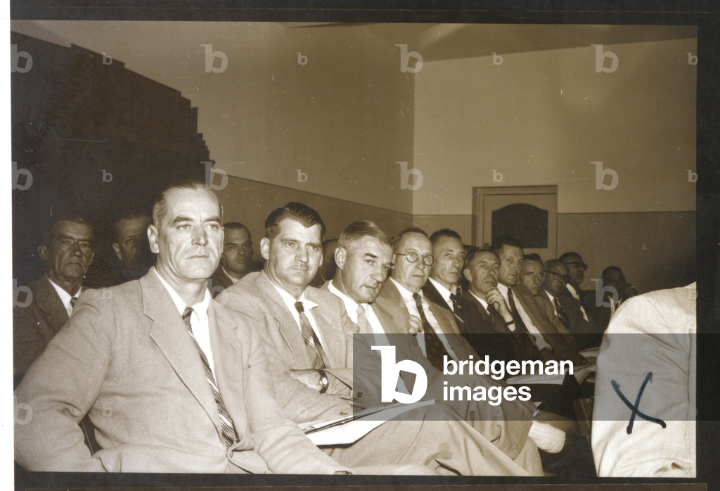 Image of White men sit in rows in a hall and appear