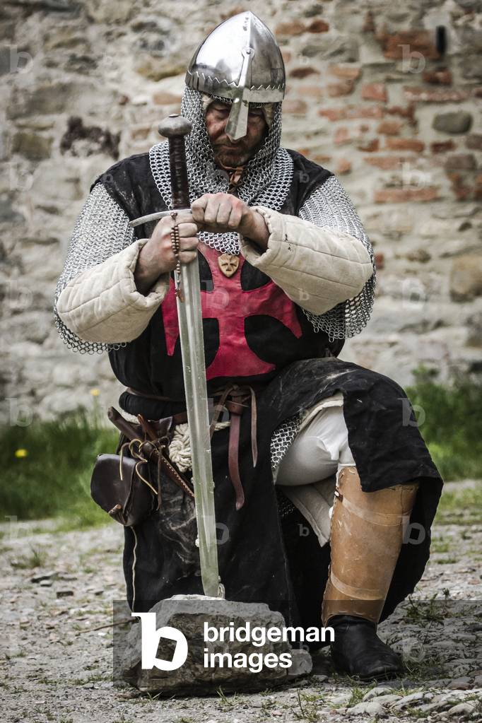 Image of Historical reenactment: Templar knight with sword kneeling in ...