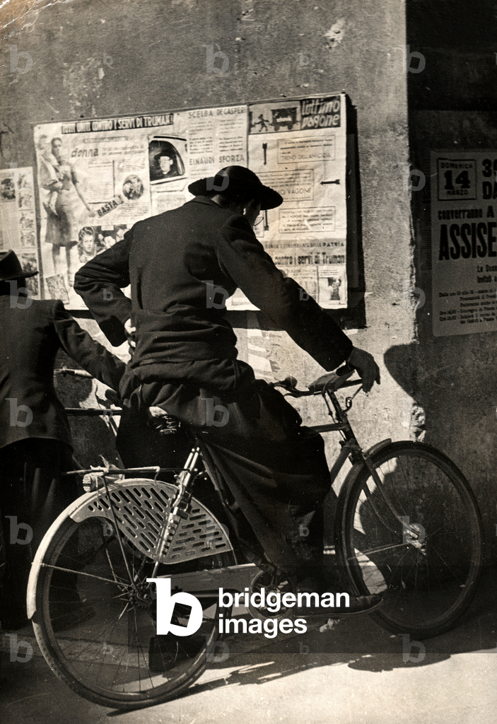 Image of A priest on a bicycle reading wall newspapers of the by Leoni ...